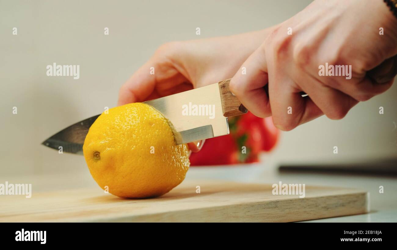 Hands with knife cutting lemon on the kitchen board. Close up shot ...