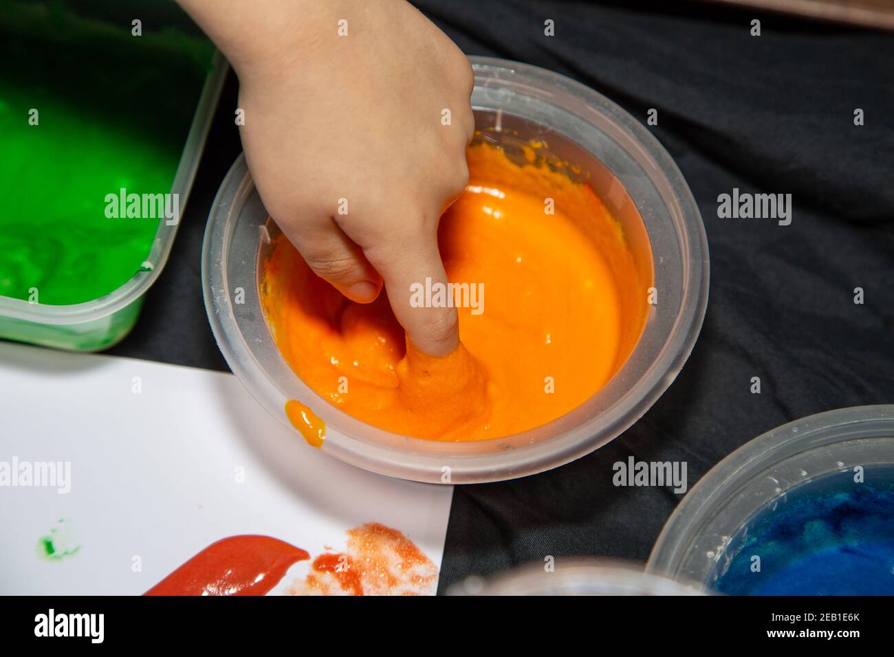a child dipping his finger into a pot of orange paint for finger ...