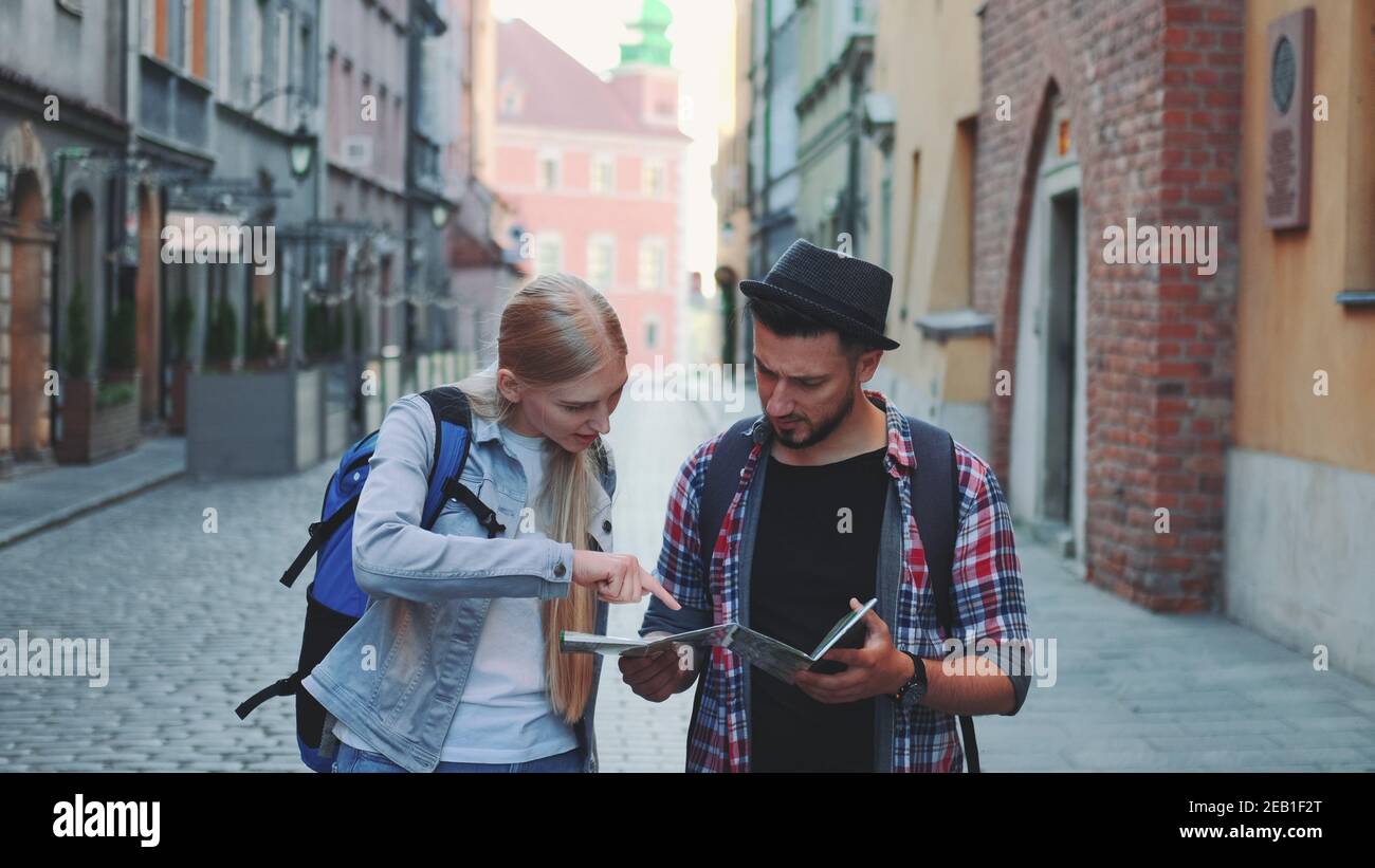 Two young tourists checking map while walking on main tourist street ...