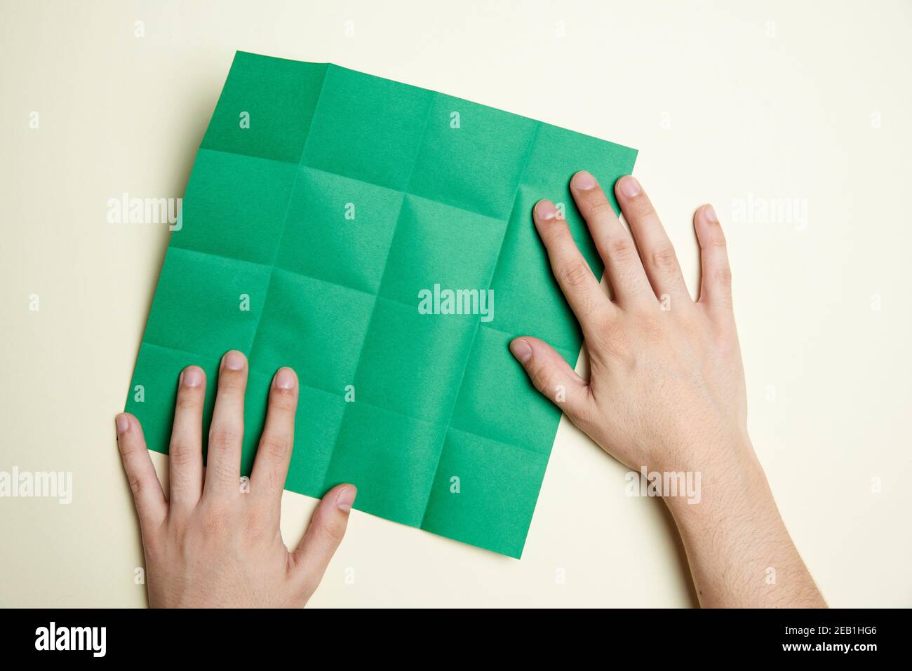Young hands and a square of green paper with marked folds, to make an ...