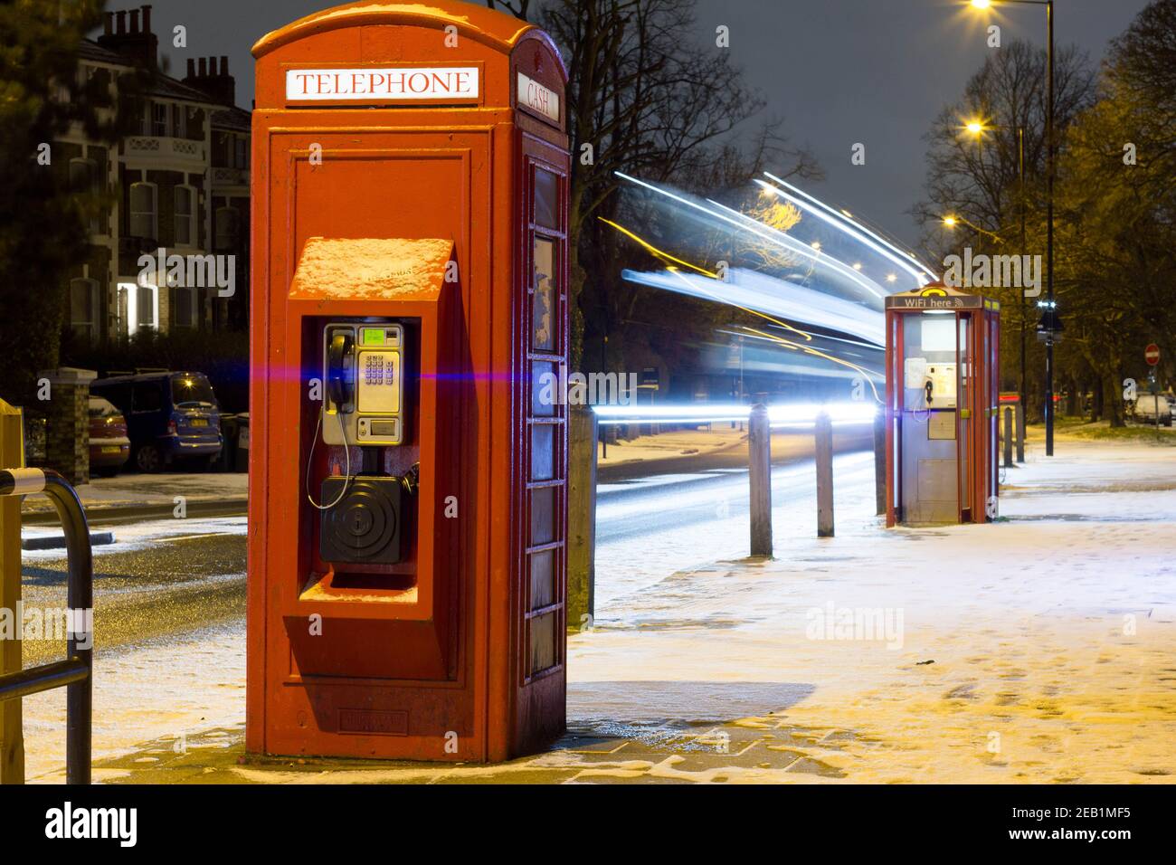 Red cast iron telephone box standing in the snow with light trails at ...