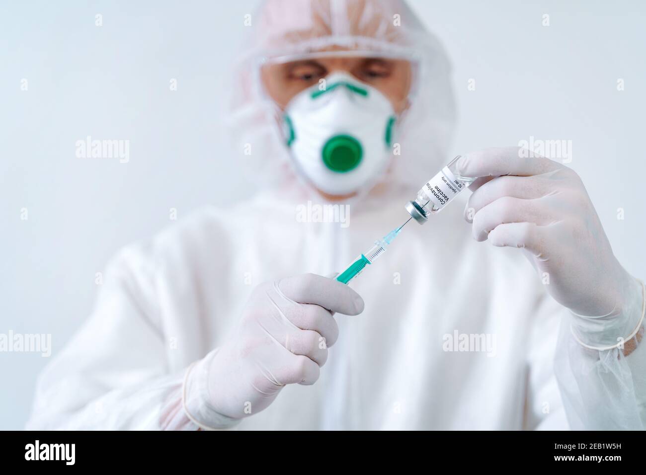 Man in protective suit and mask holds an injection syringe and vaccine ...