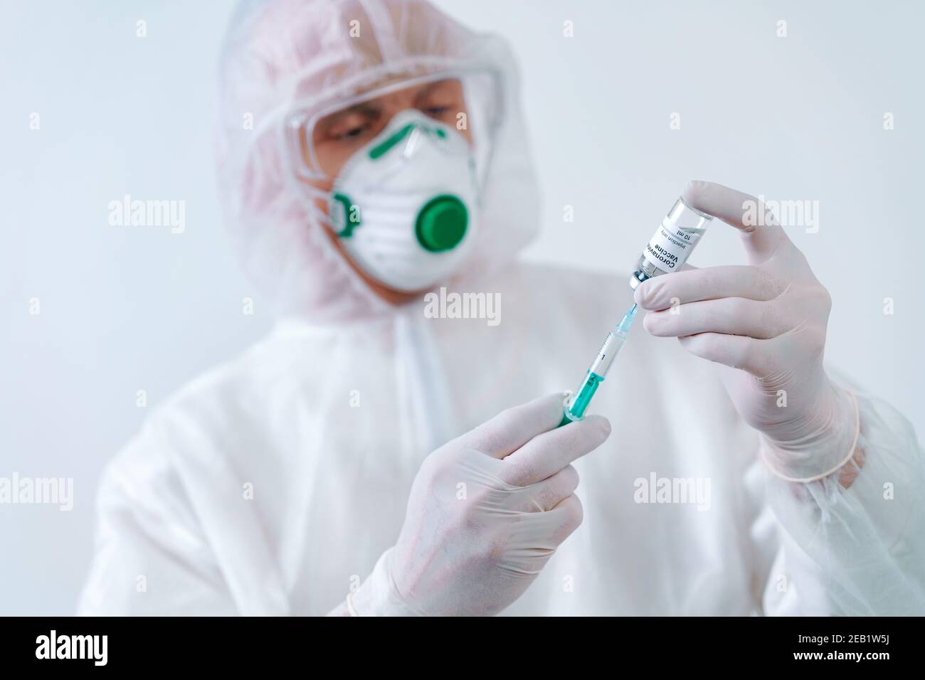 Man in protective suit and mask holds an injection syringe and vaccine ...