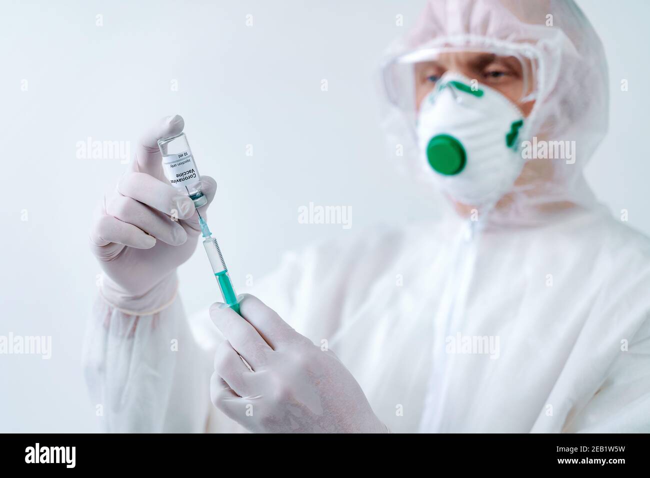 Man in protective suit and mask holds an injection syringe and vaccine ...