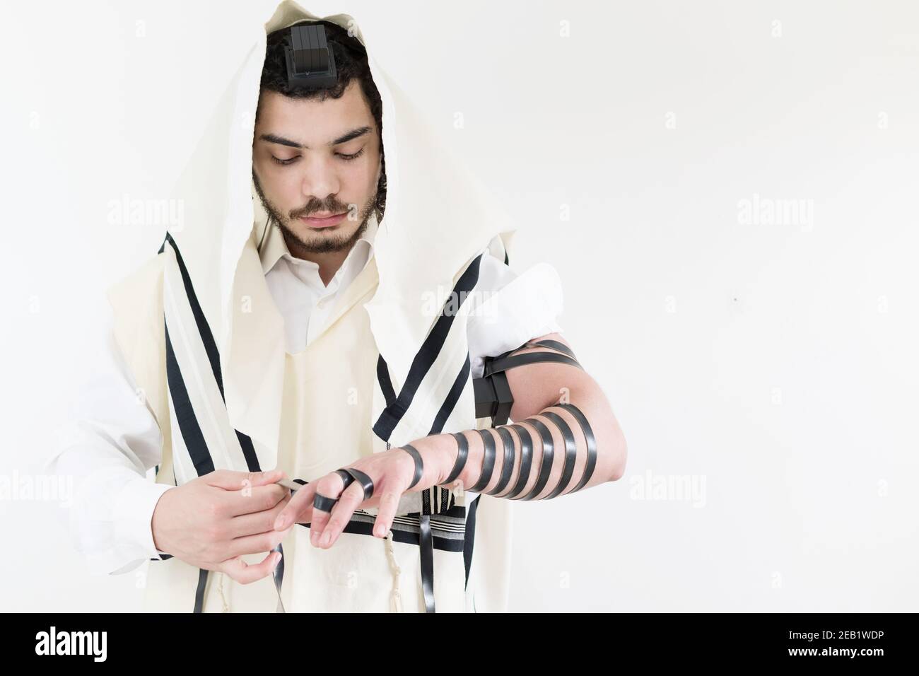 Young Orthodox Jew in shawl (tallit) putting on phylacteries (tefillin ...