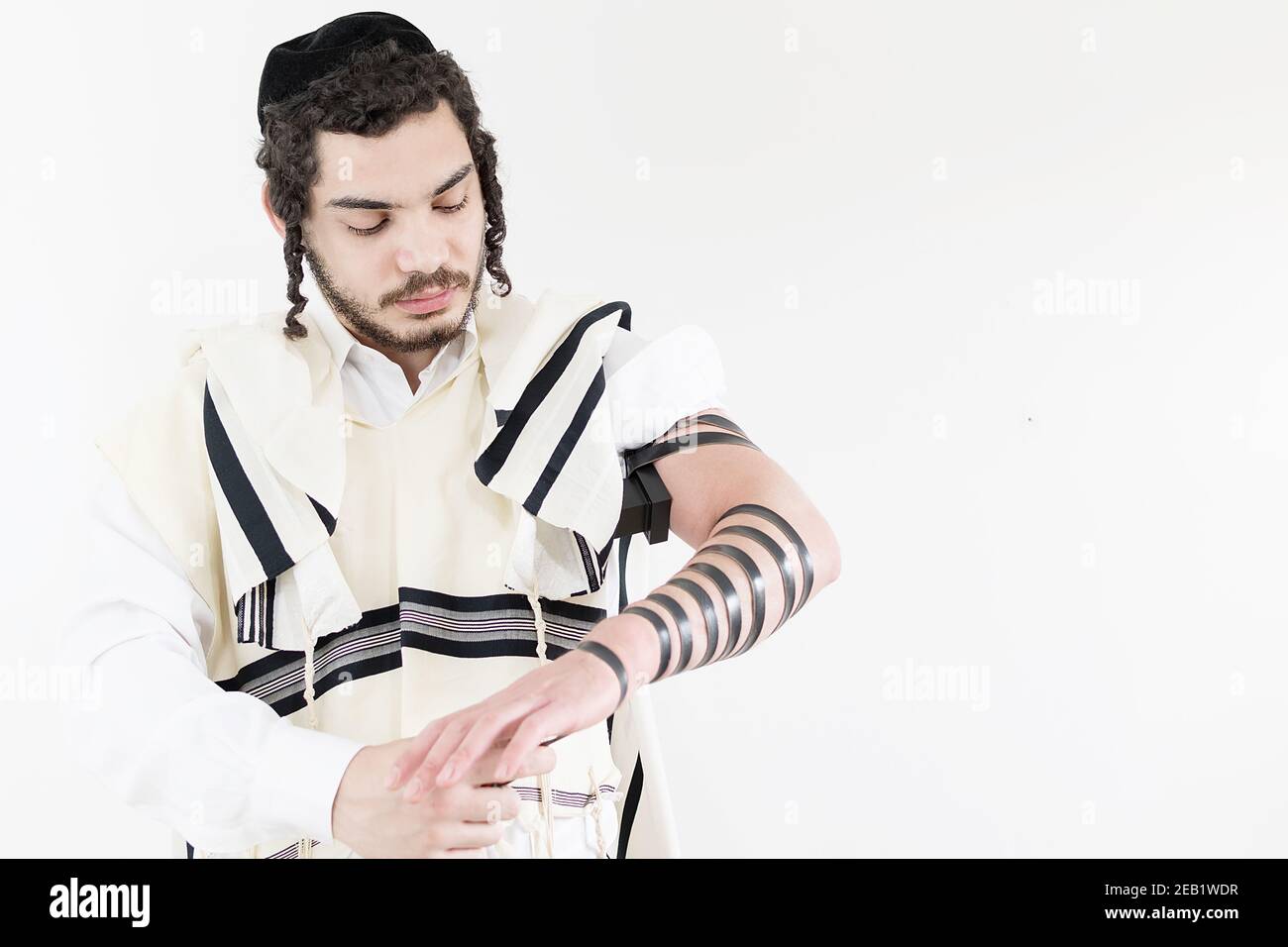 Young Orthodox Jew in shawl (tallit) putting on phylacteries (tefillin ...