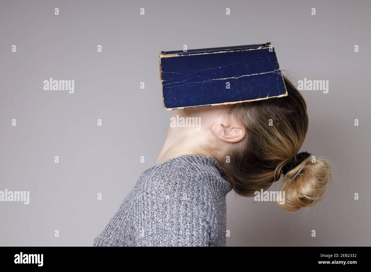 A beautiful woman in a gray sweater, hiding her face behind a book ...