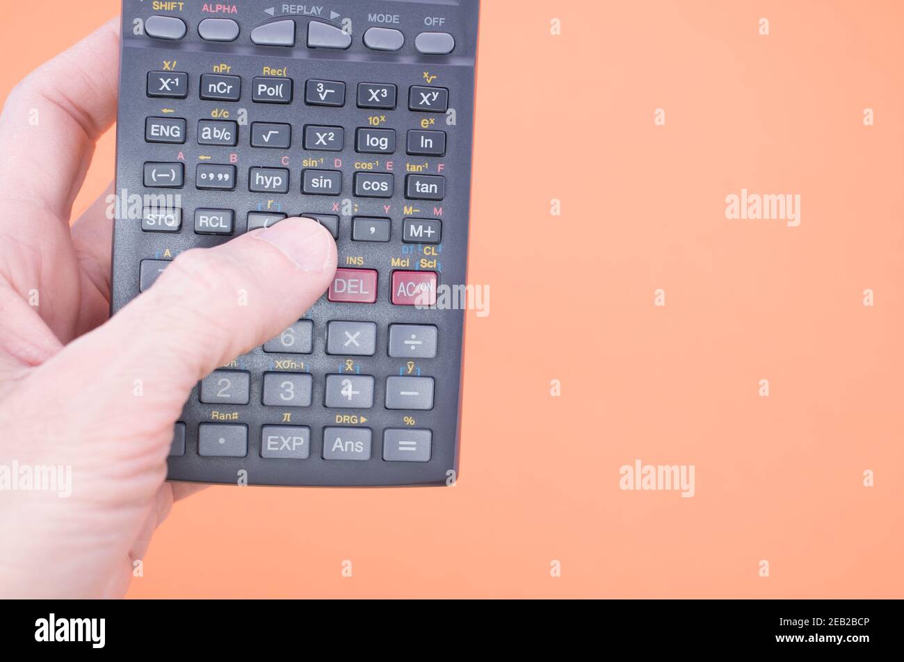 A scientific calculator on a person's hand against an orange background ...