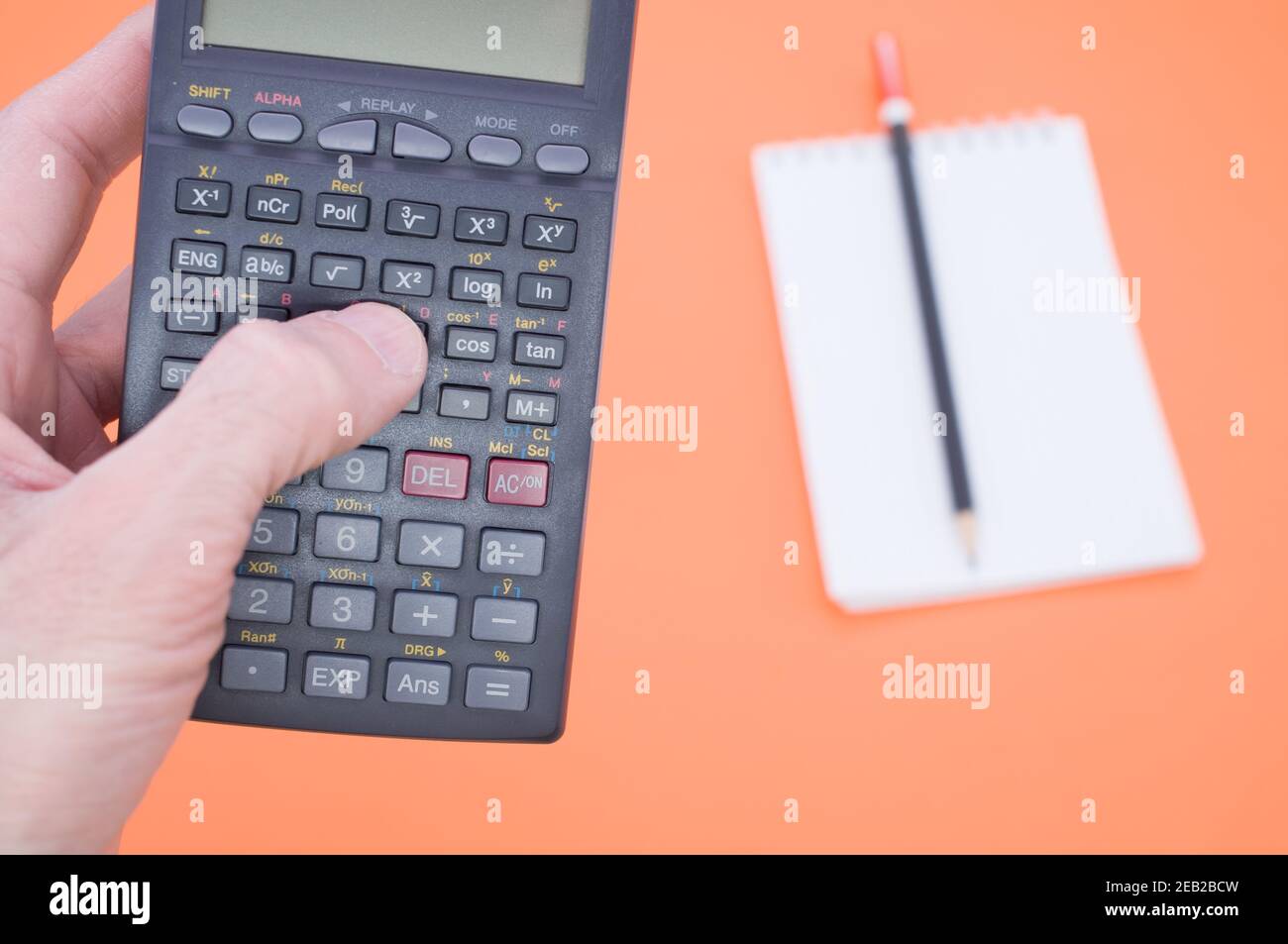A scientific calculator on a person's hand against with a notepad and ...