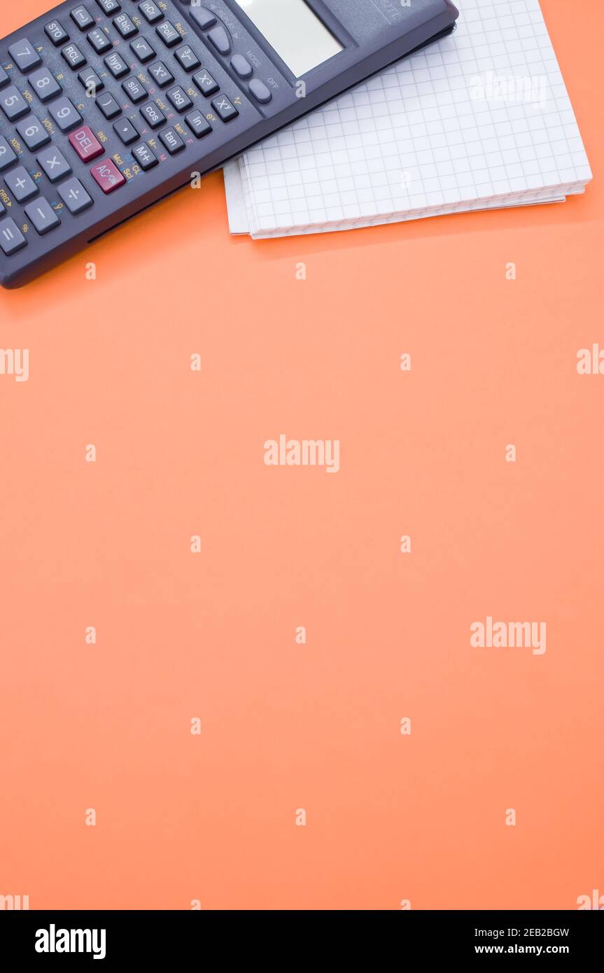 Vertical shot of a scientific calculator and a notepad on orange ...