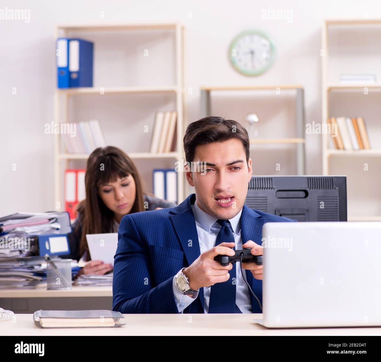 The man playing games in office while colleague is busy Stock Photo - Alamy