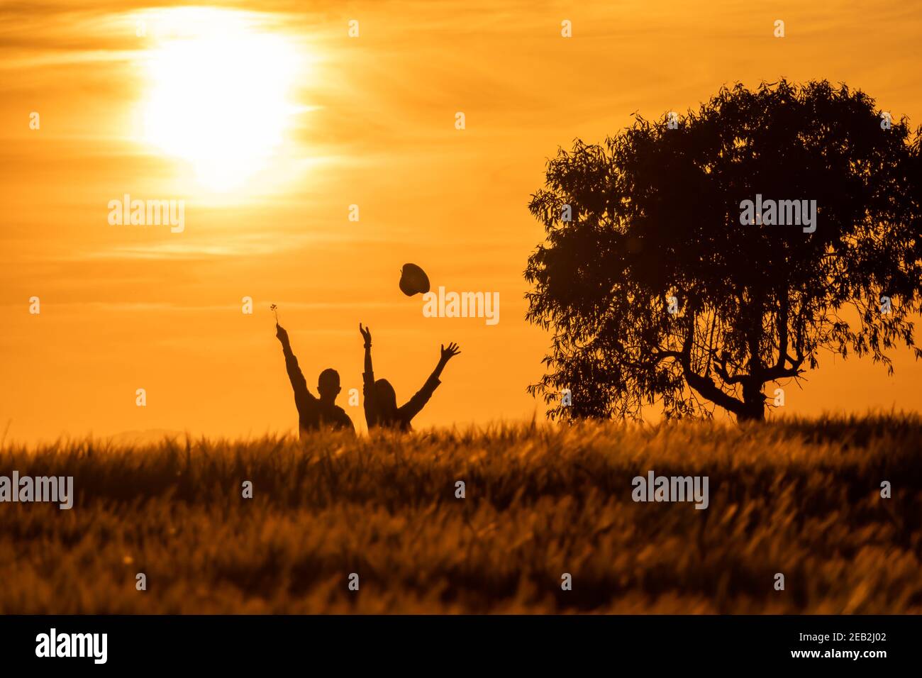 silhouette of girl and boy tossing hats in the air at a sunset in the ...