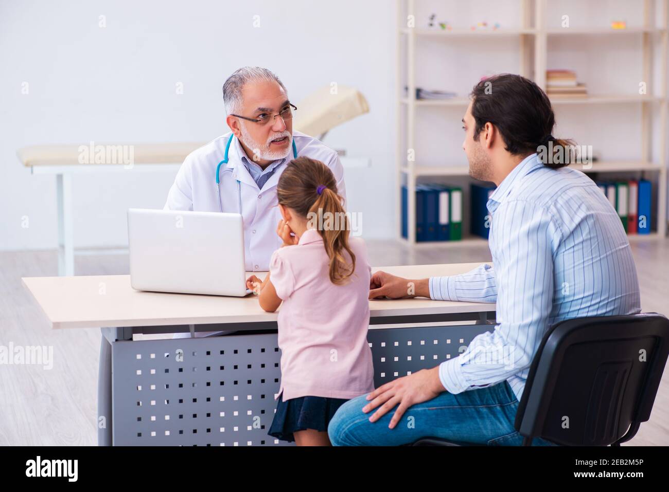 Little girl with her father visiting old male doctor Stock Photo - Alamy