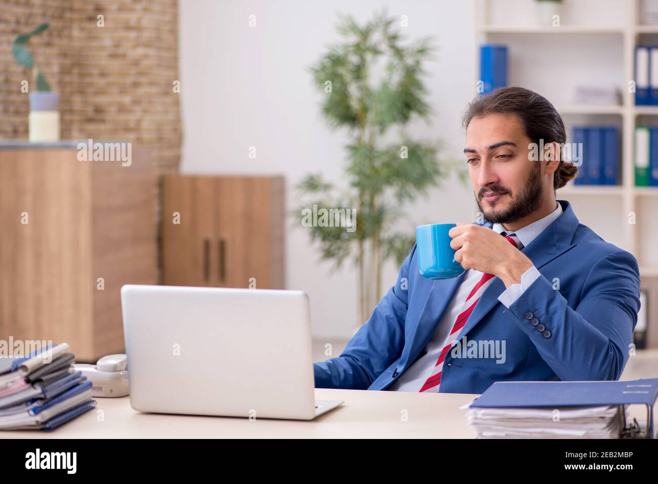 Young employee drinking coffee at workplace Stock Photo - Alamy