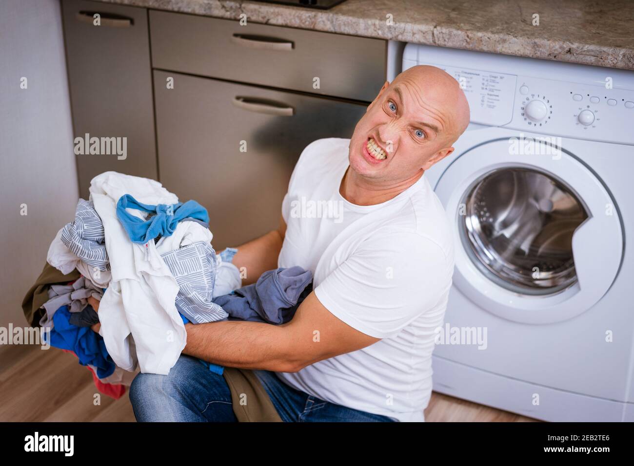 tired bald man sitting with dirty laundry in the washing machine ...