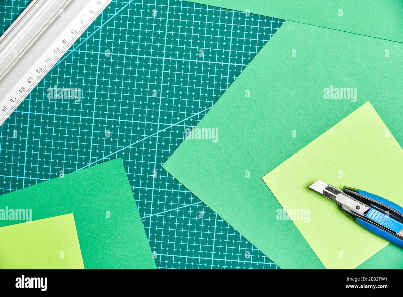 Green sheets of paper, a metal ruler and a cutter on a cutting mat ...