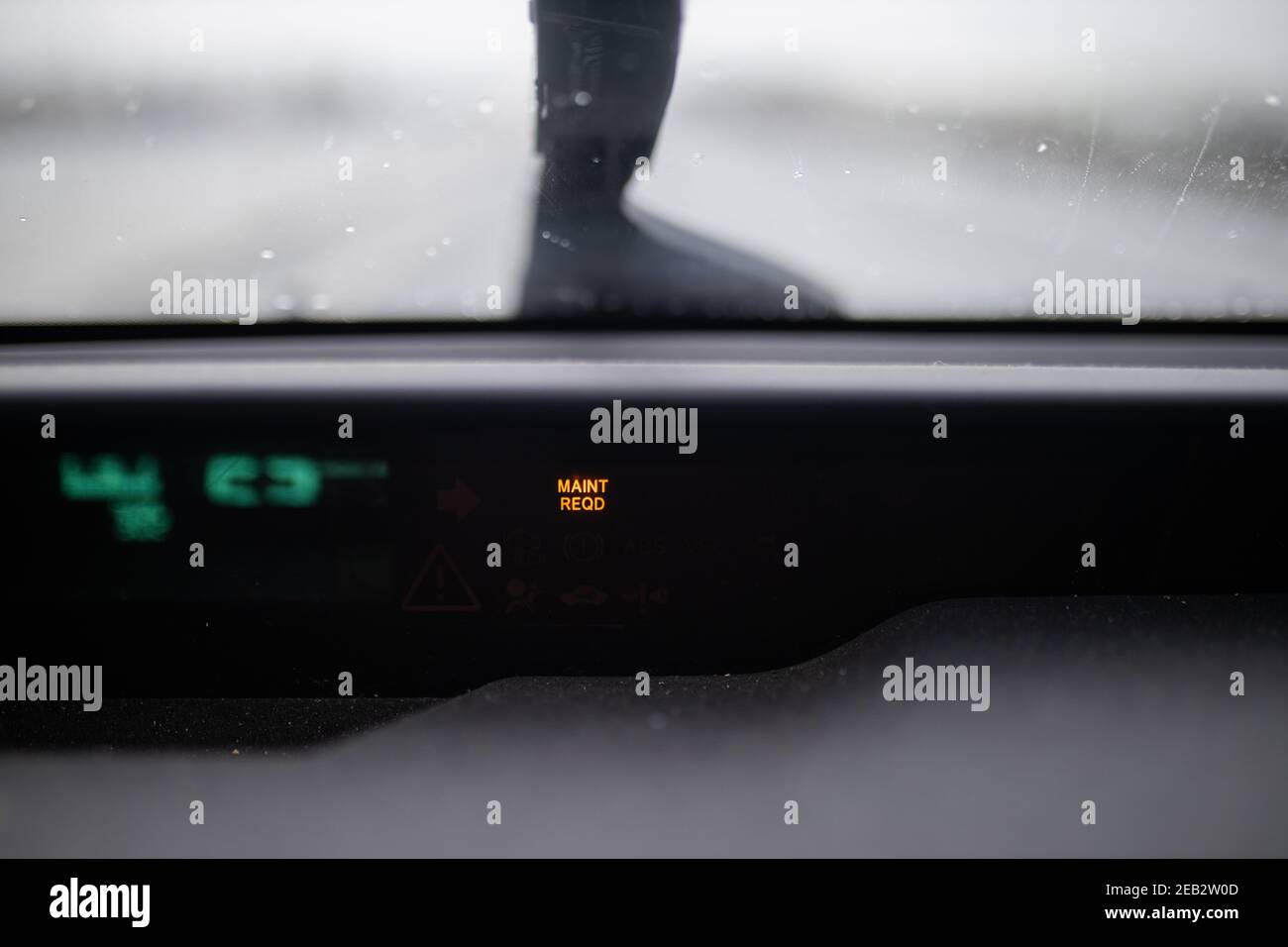 Maintenance required light shining on dashboard under a wet windshield ...