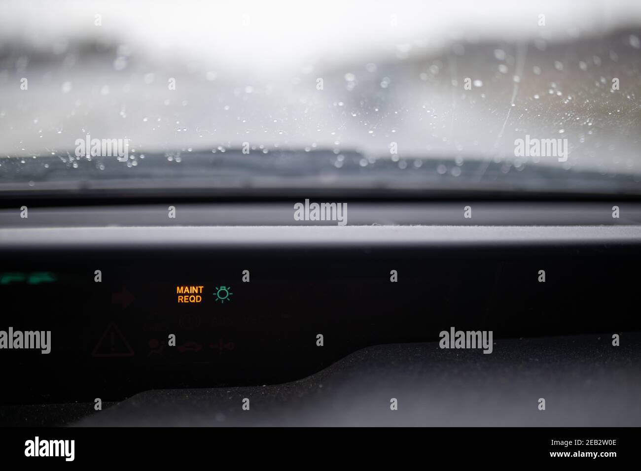 Maintenance required light shining on dashboard under a wet windshield ...