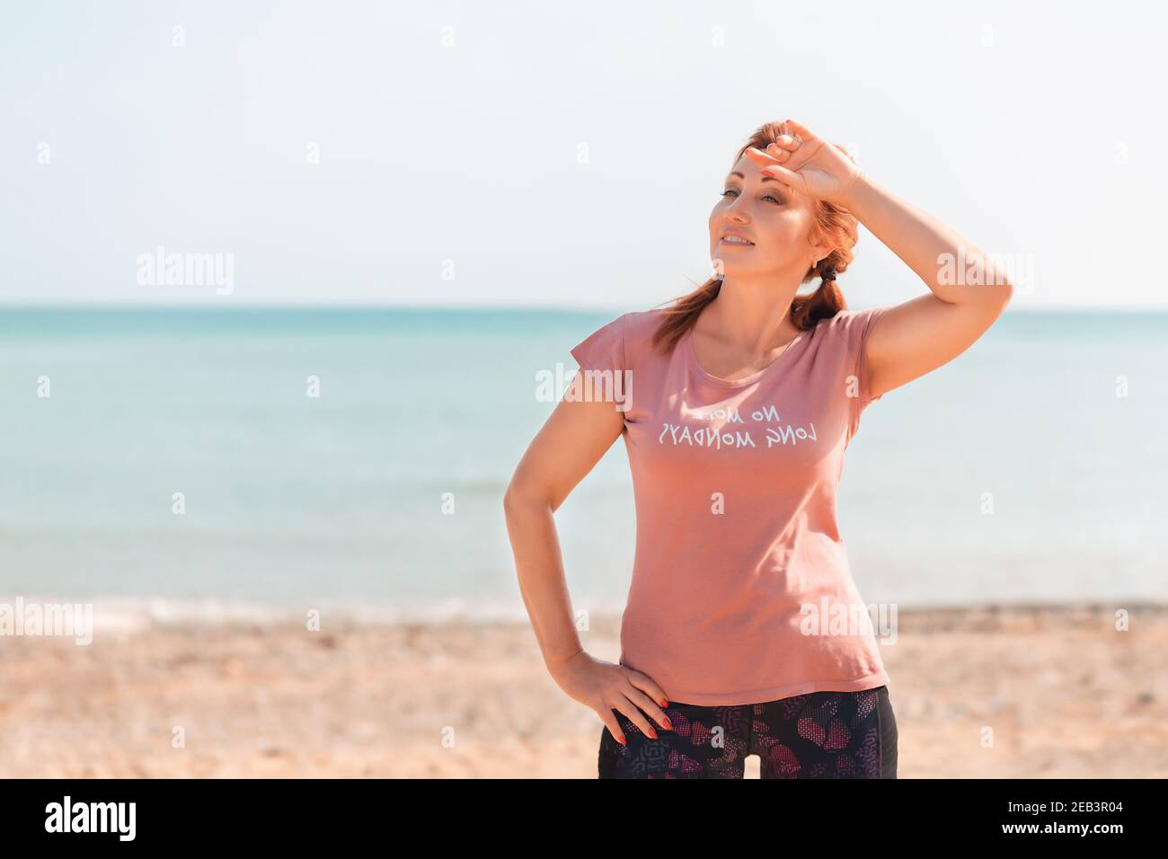 A beautiful adult woman poses on the beach, wiping the sweat from her ...