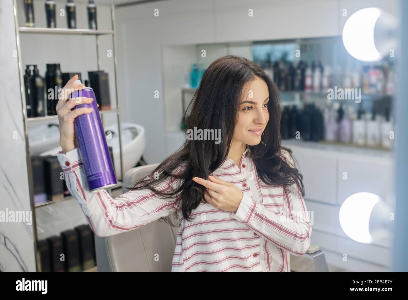 Long-haired young brunette spreading some hair spray on her hair Stock ...