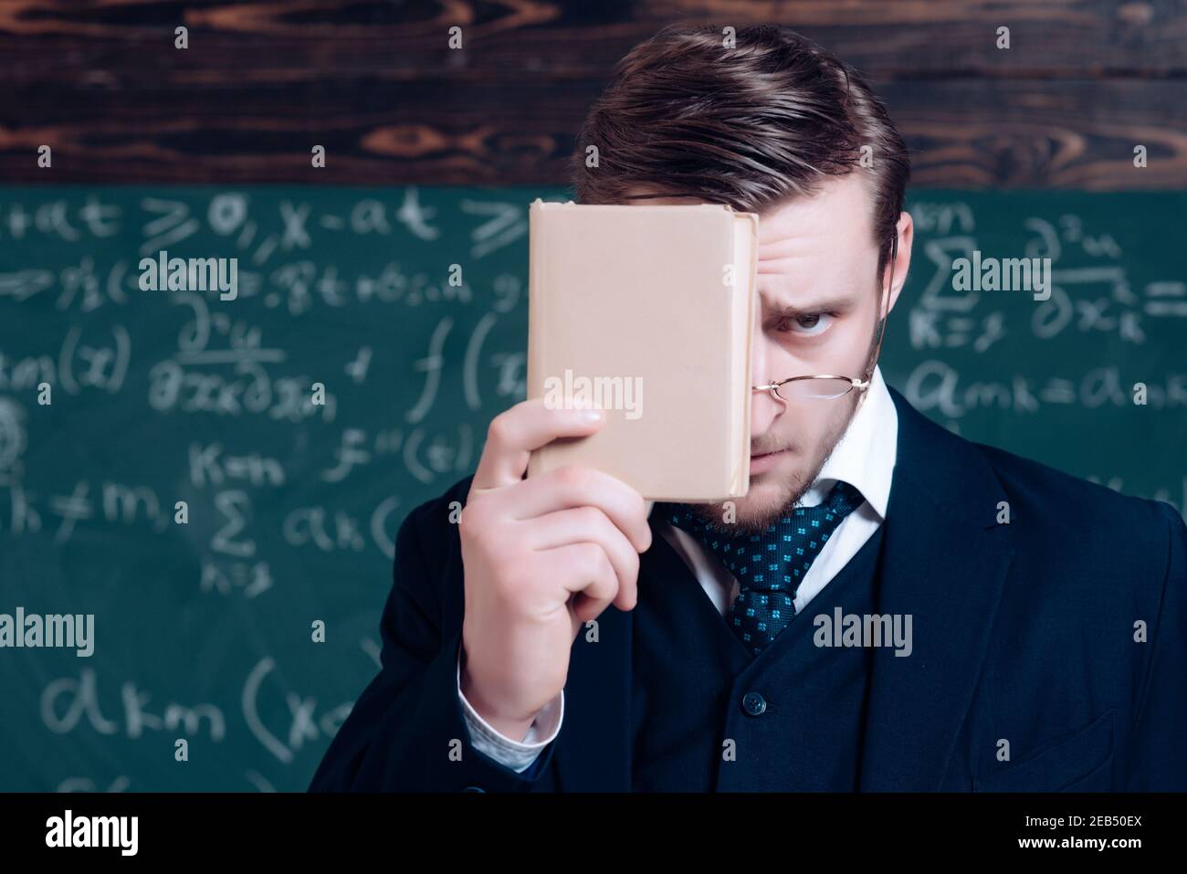 Young teacher in suit covering his face with book. Closeup portrait of ...