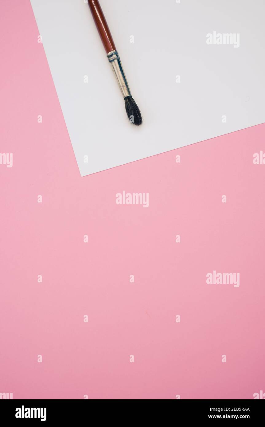 Vertical top view of a paintbrush and a paper isolated on a pink ...