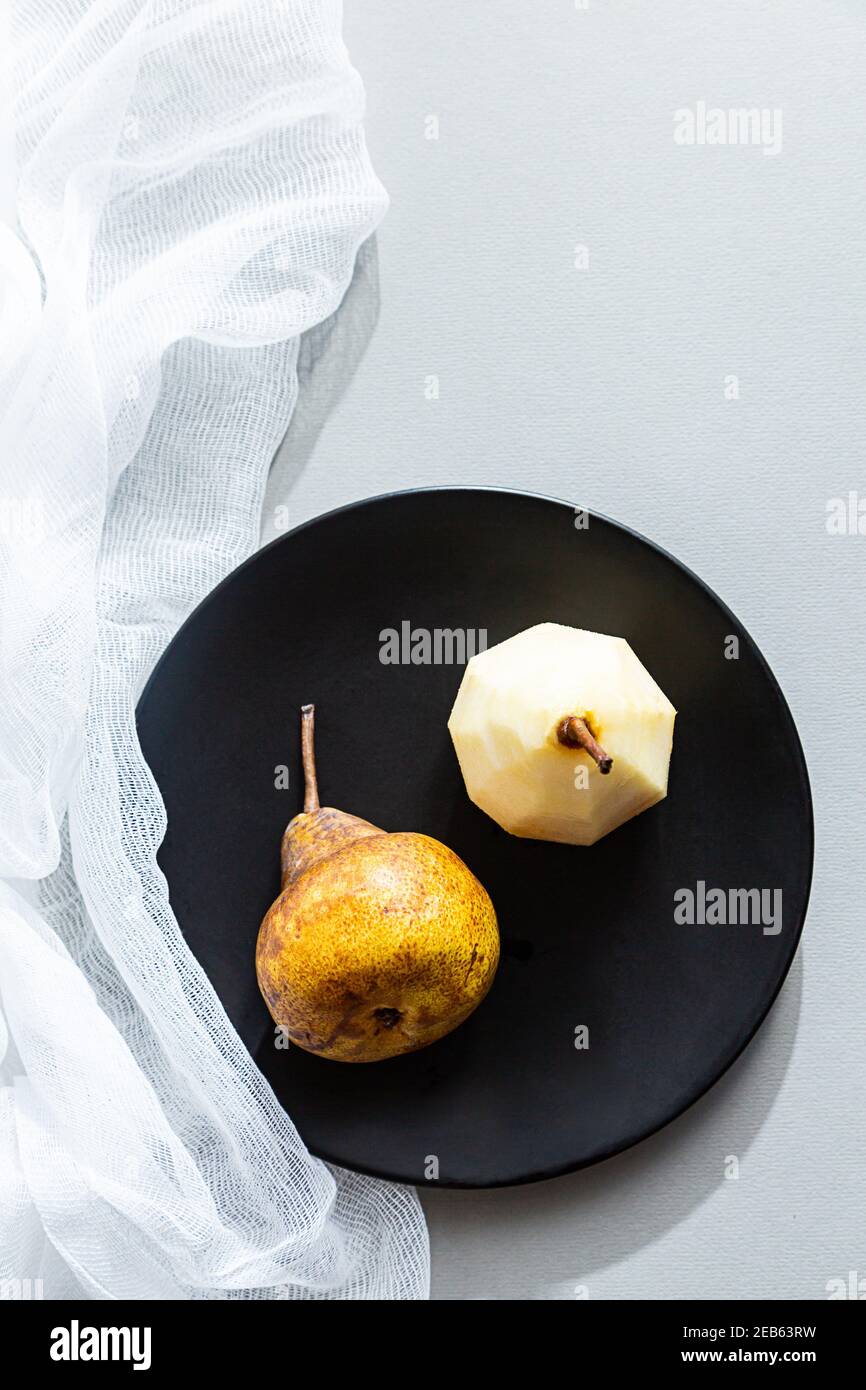 Modern still life, whole and peeled pears in a black plate on a gray ...