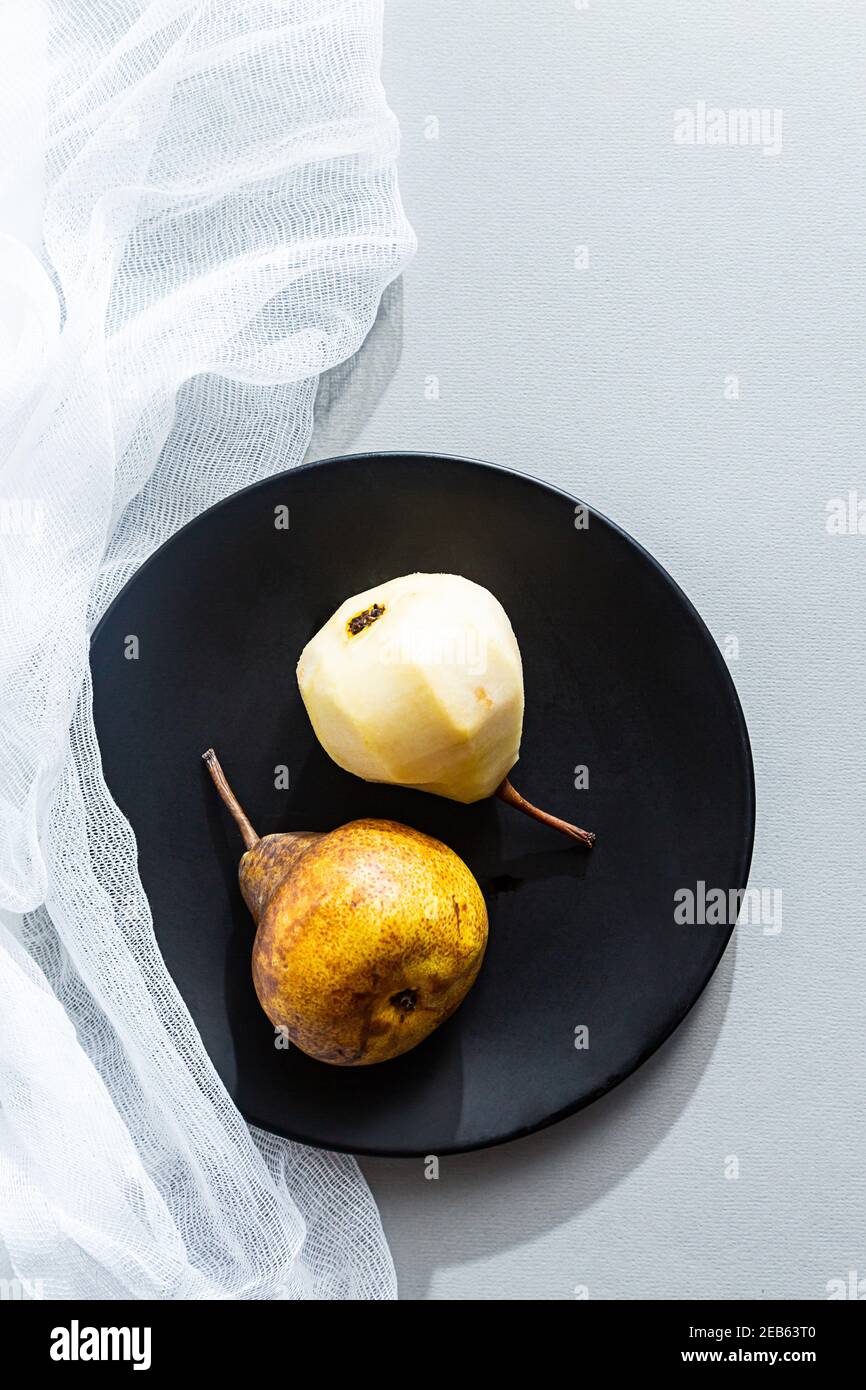 Modern still life, whole and peeled pears in a black plate on a gray ...