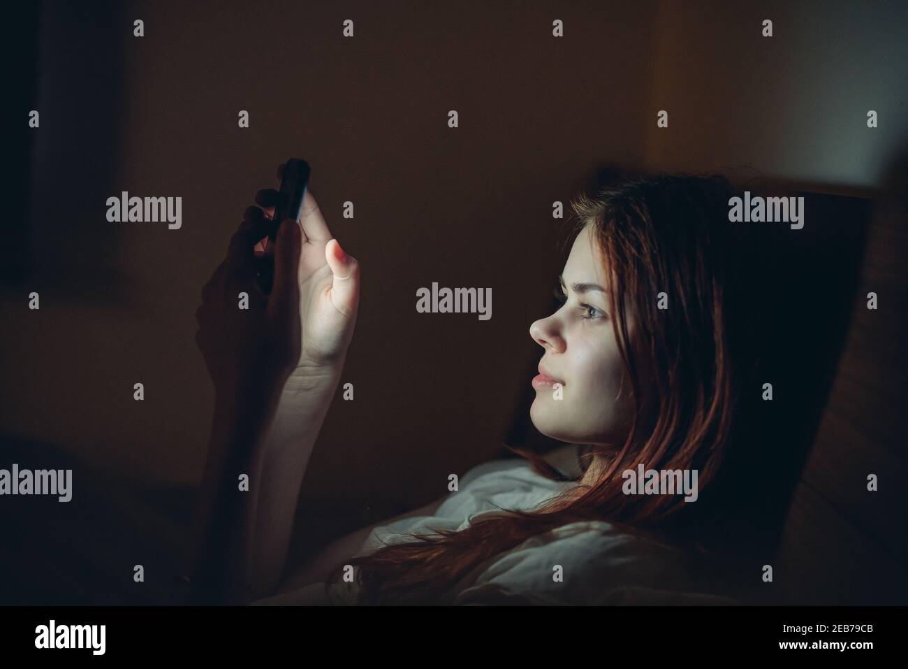 pretty woman lying in bed with phone in hand at night rest before ...