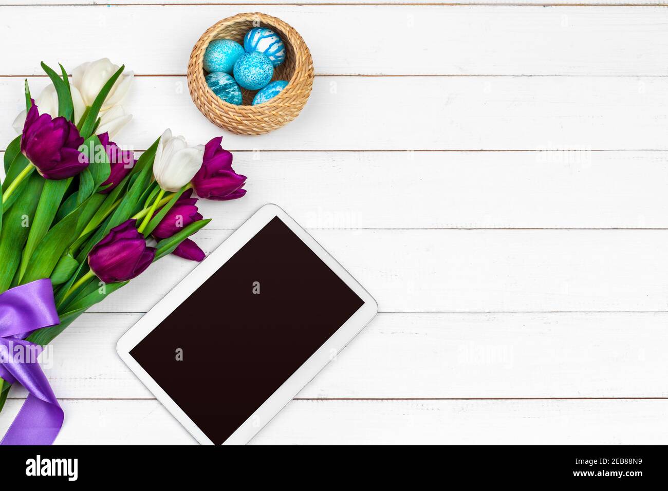 tablet screen for message and colorful tulips and easter eggs on wooden ...