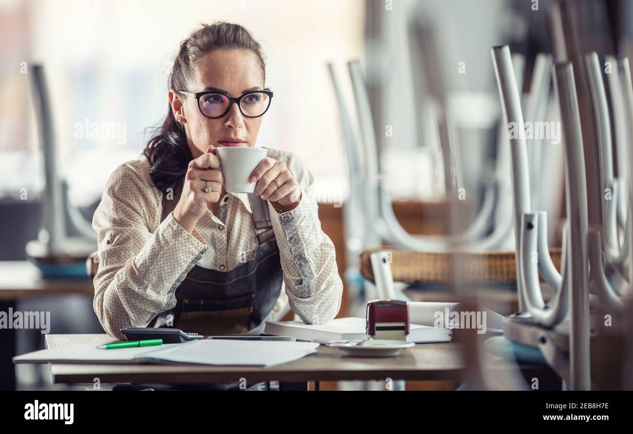 Business owner sips coffee sitting over accounting of her closed bar or ...