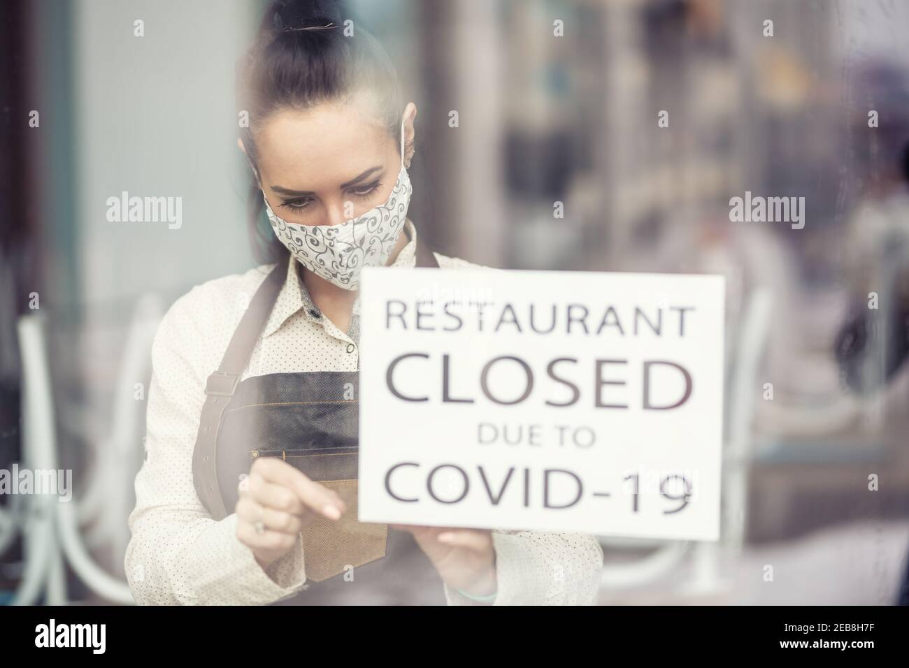 Waitress is sticking sign saying restaurant closed due to covid-19 on a ...