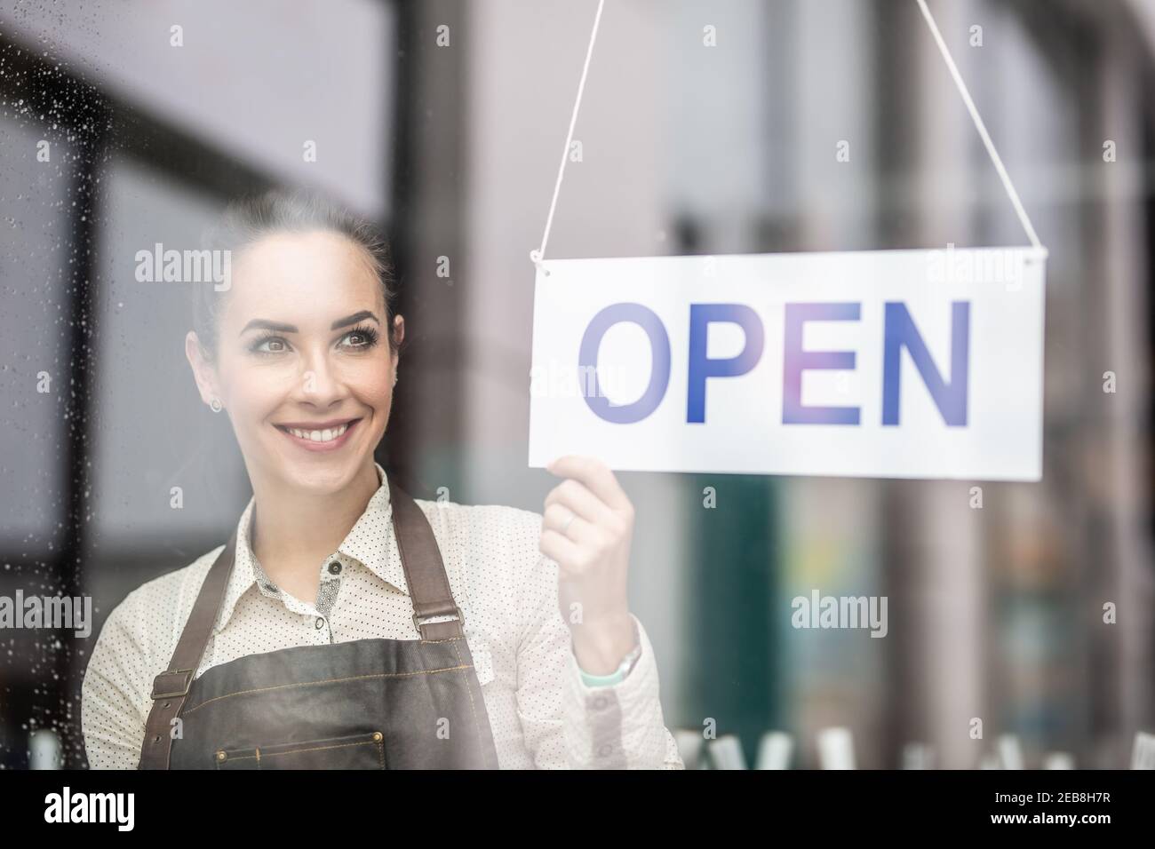 Smiling beautiful waitress turning the sign open on a restaurant or a ...