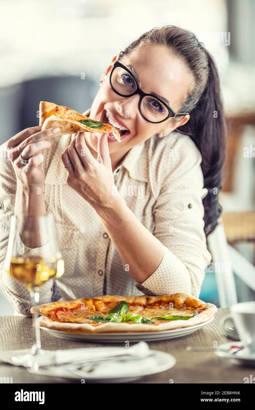 Cute young woman tilts her head as she bits into a slice of pizza Stock ...