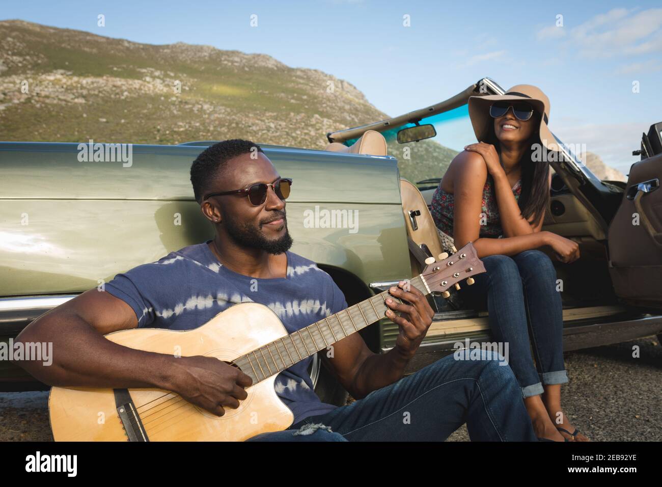 Diverse couple taking roadside break on sunny day beside convertible ...