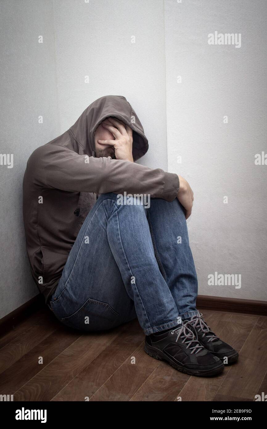 desperate young drug addict wearing hood and sitting alone in corner ...