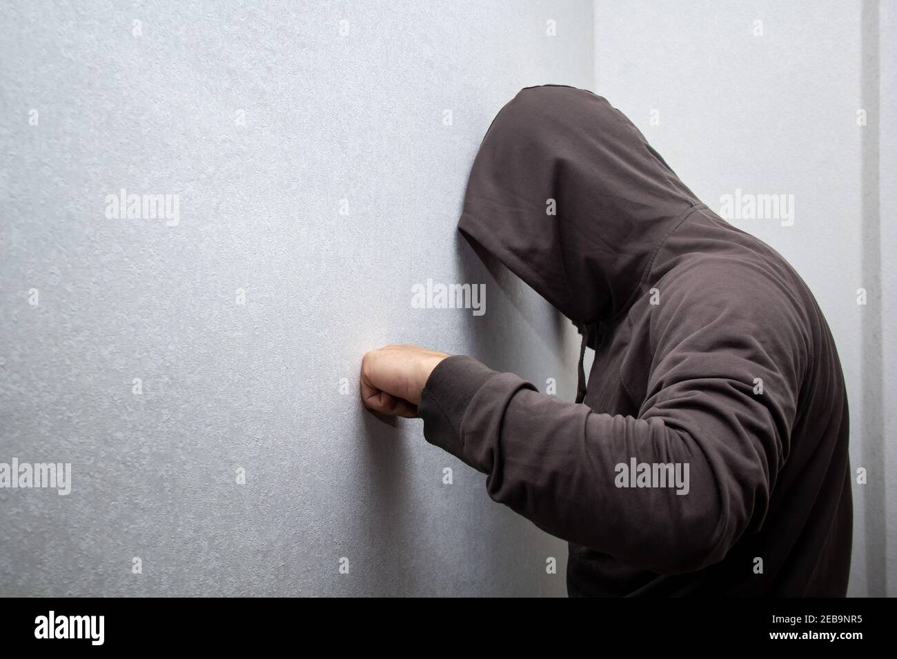 angry man in a gray hood slams his fist against the white wall Stock ...