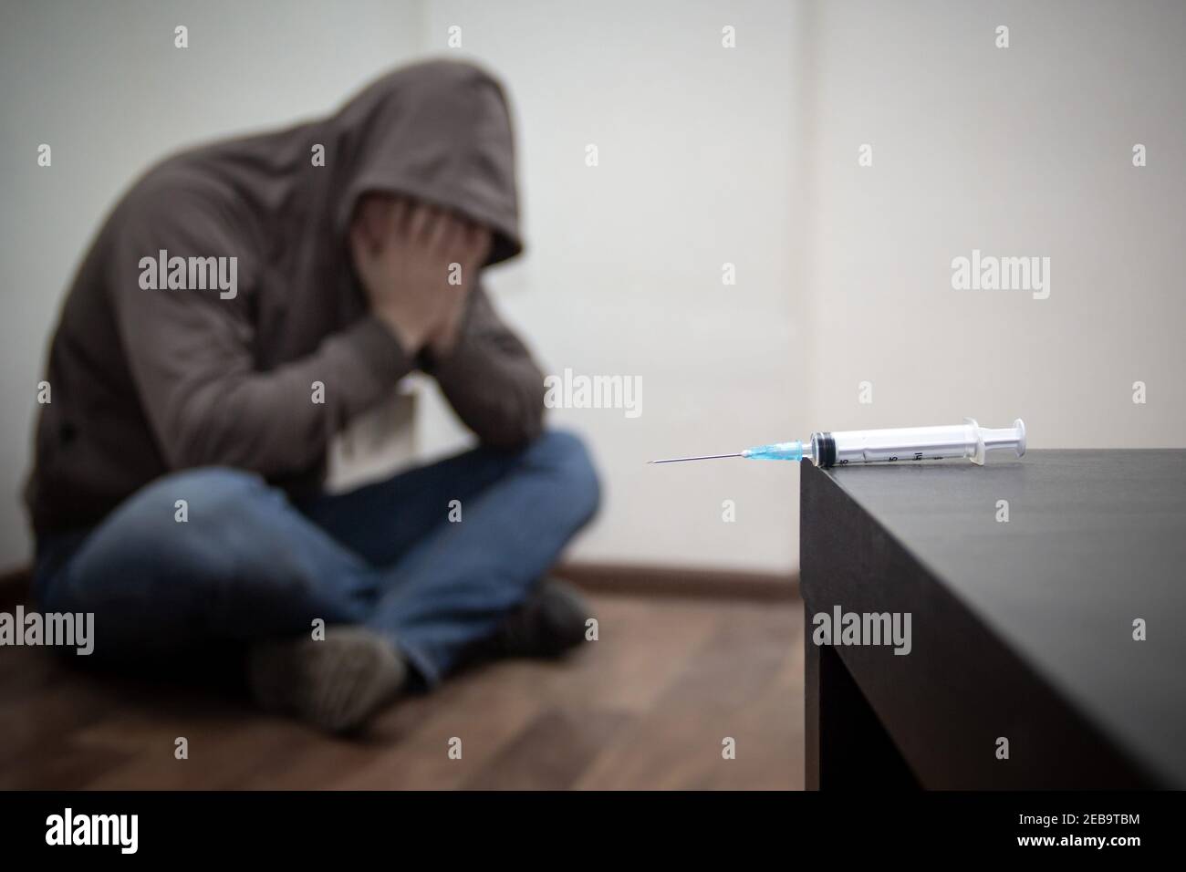 Syringe and man drug addict without of focus sitting in corner in the ...