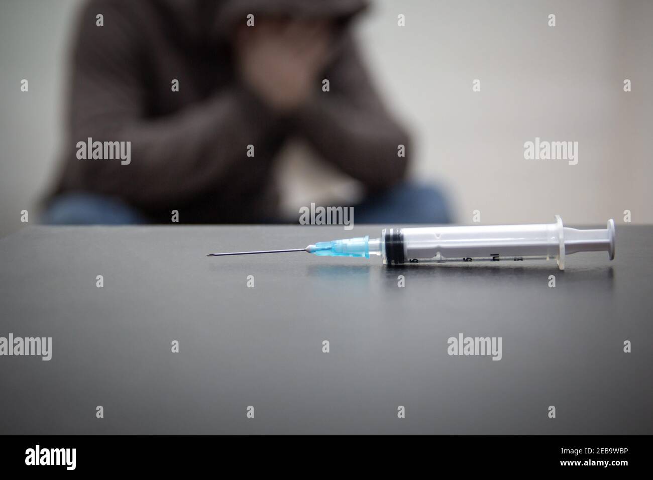 Syringe and man drug addict without of focus sitting in corner in the ...