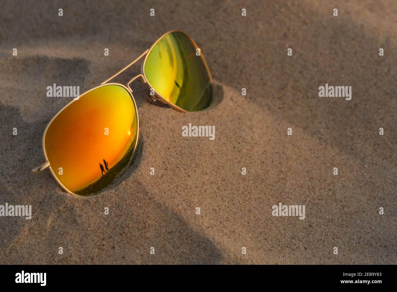 Mirrored sunglasses close up on beach sand with sundown and couple ...