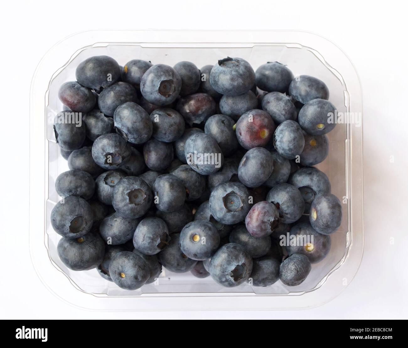 Plastic punnet full of lush blueberries against plain white background ...