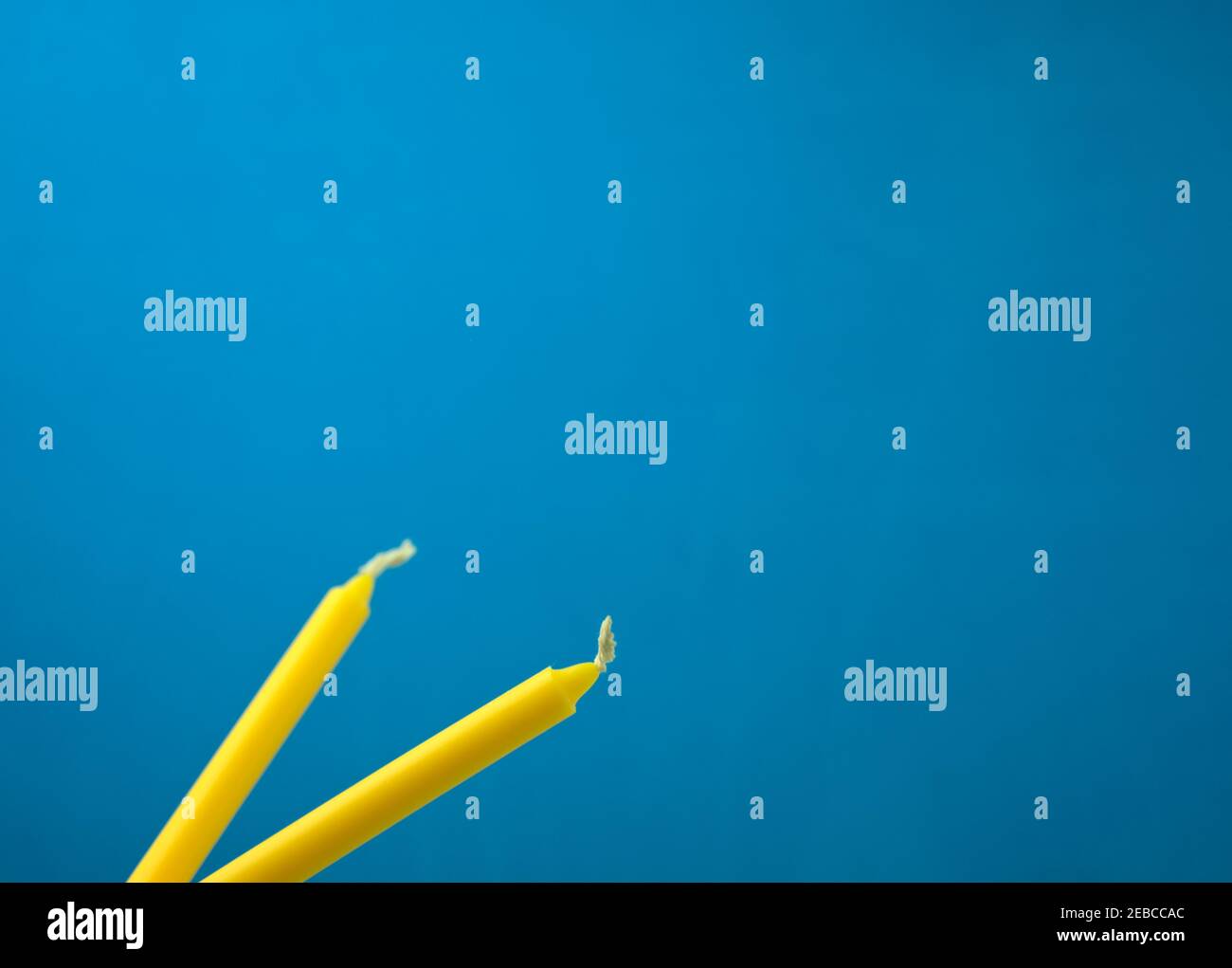 Bright yellow candles isolated on blue background. Off-center, head on ...