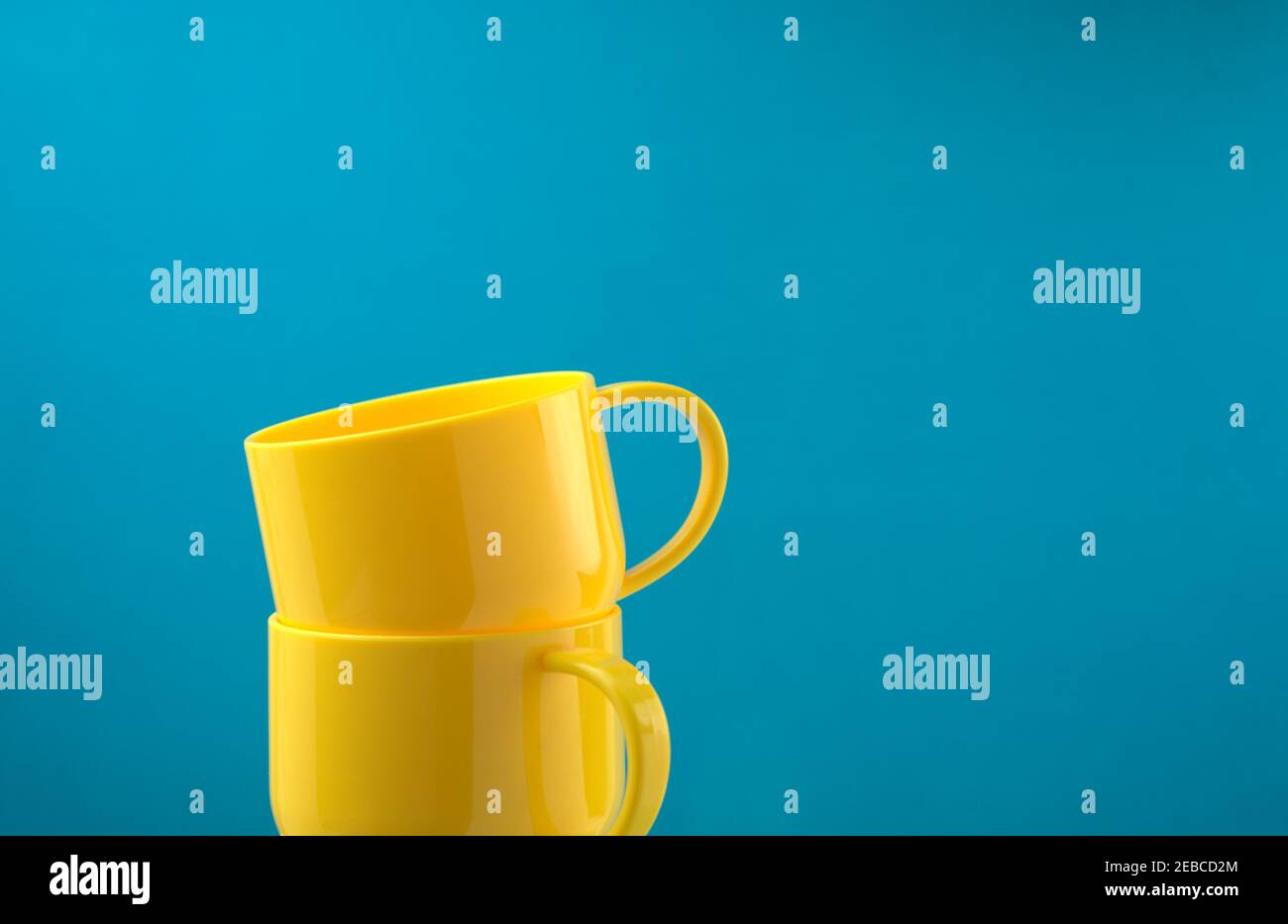 Glossy yellow colored cups stacking on blue background. Off-center ...