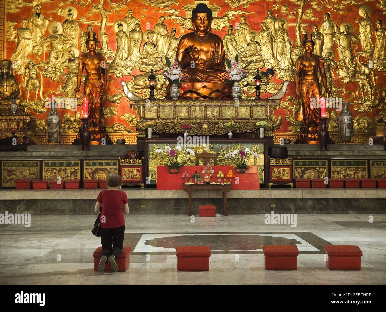 A Chinese woman kneeling in front of Buddha's altar while offering ...