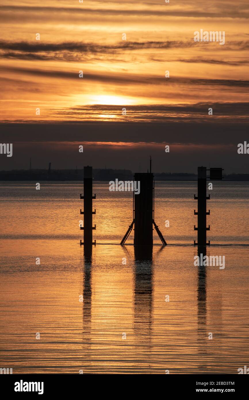Vertical shot of dock base silhouettes on the sea under a cloudy sky ...