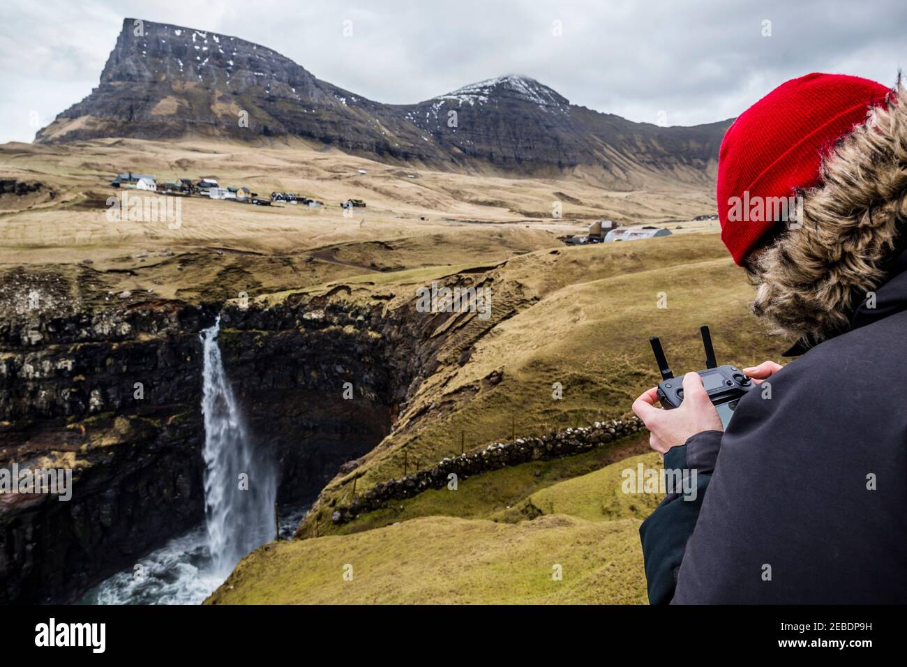 Pilot flying his drone (uav) above Mulafossur Waterfall on Vagar Island ...
