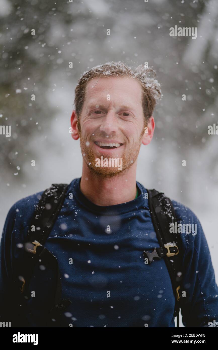 Portrait of man wearing backpack smiling with snow in hair Stock Photo ...