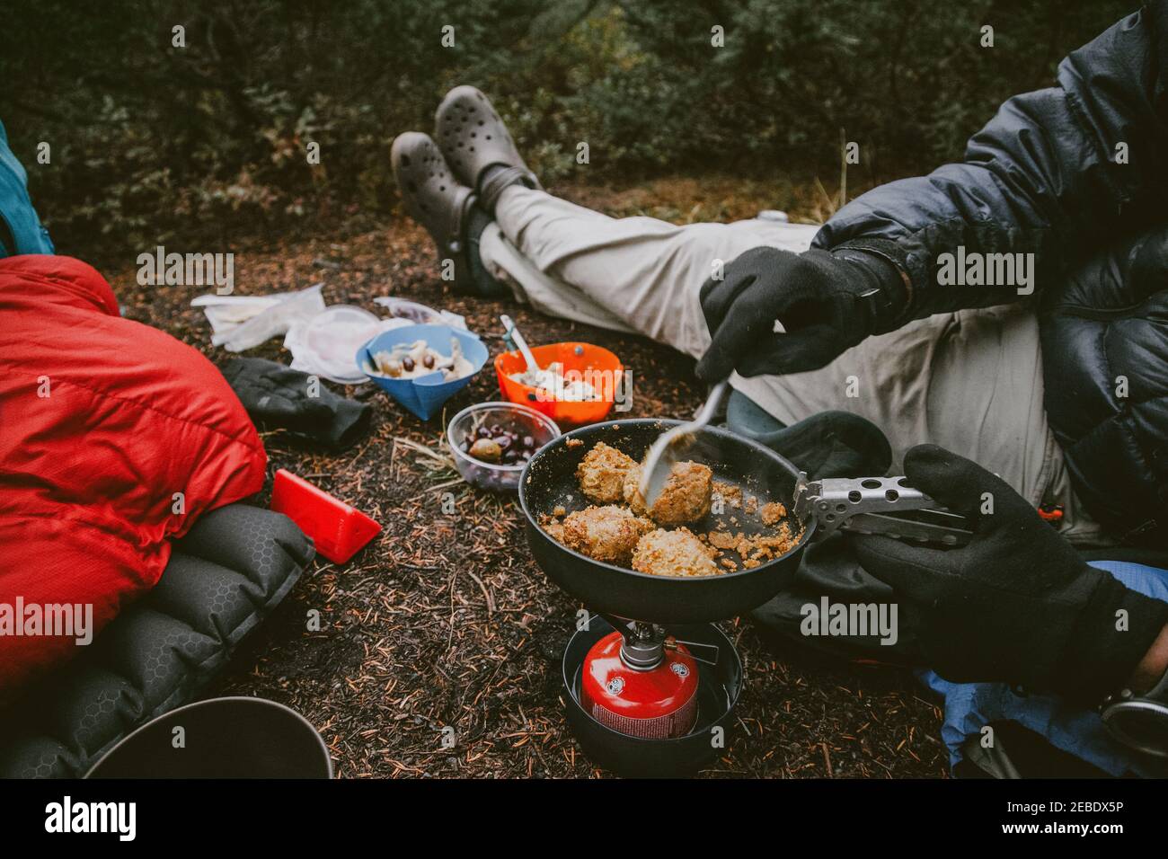 A man cooks dinner on the ground while backpacking wearing gloves Stock ...