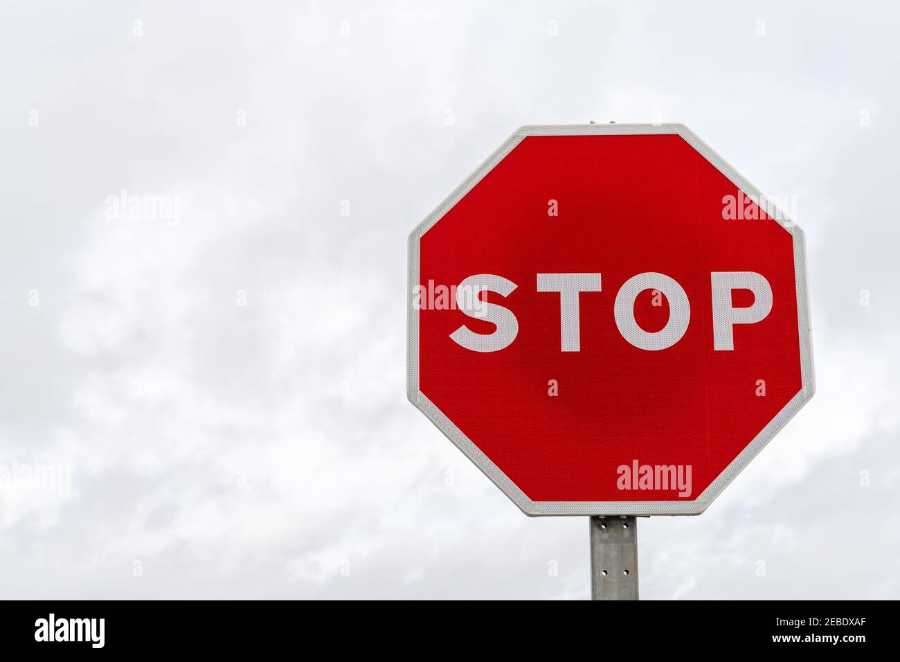 A horizontal view of a bright red stop sign with a gray overcast sky ...