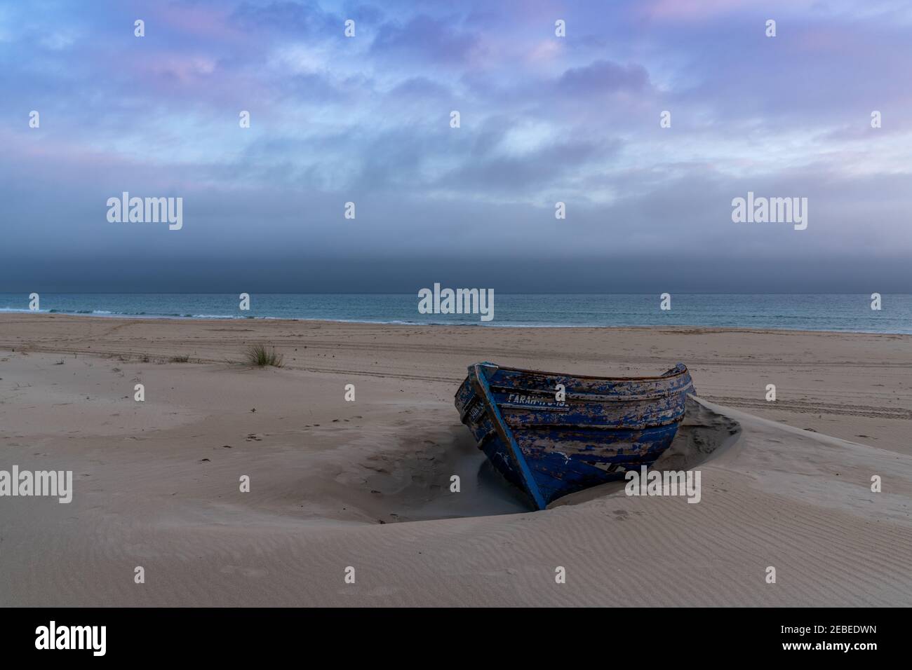 colorful wreck of an old wooden rowboat buried in the sand with a ...